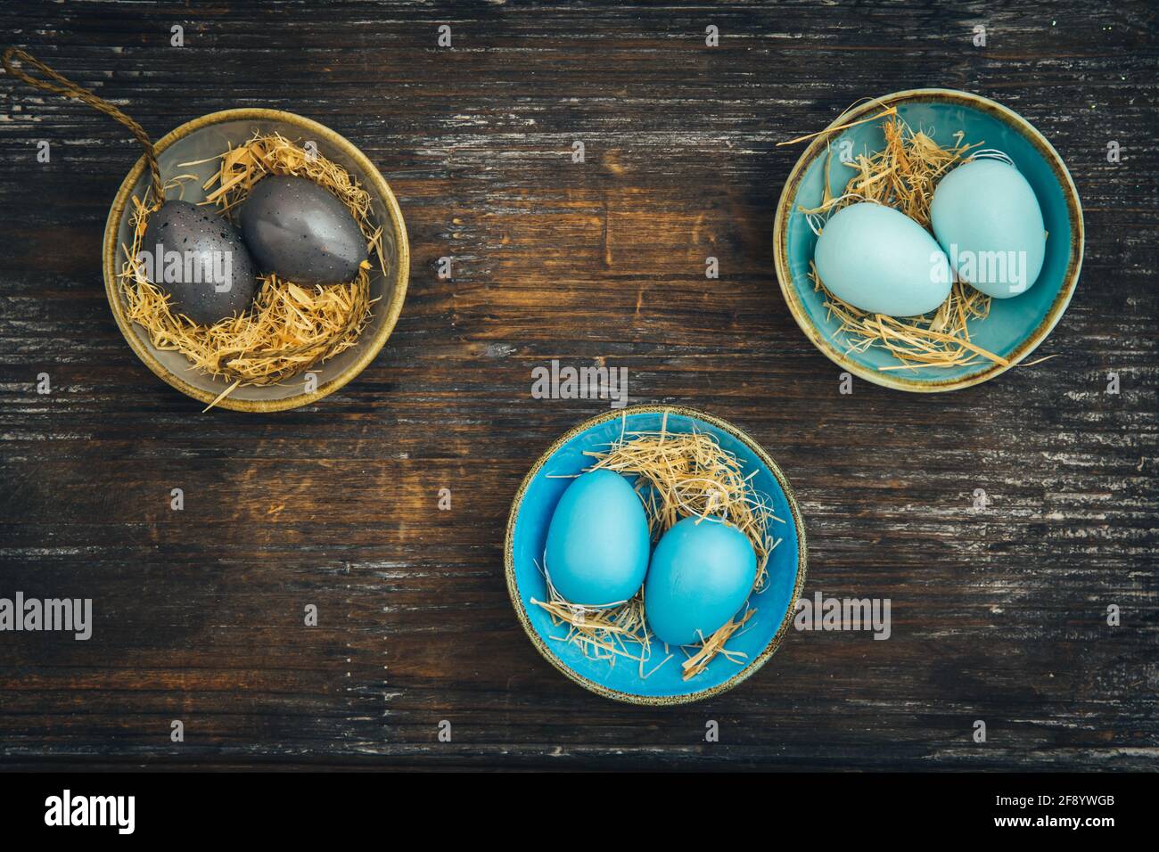 Three small colorful bowls filled with Easter eggs in the same color on ...