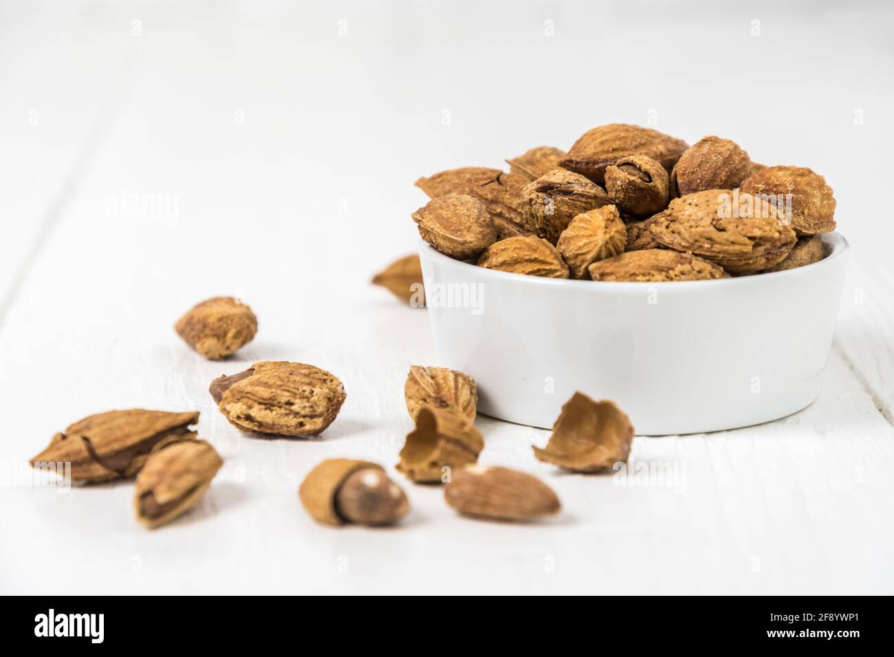 Roasted and salted snack almonds with shell in a small white bowl on ...