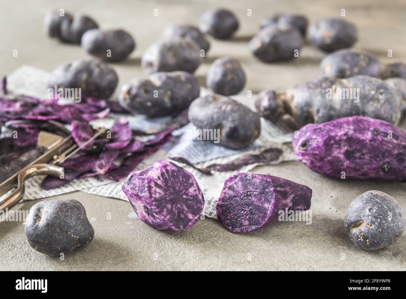 Whole and halfed peeled purple potatoes on a grey background Stock ...