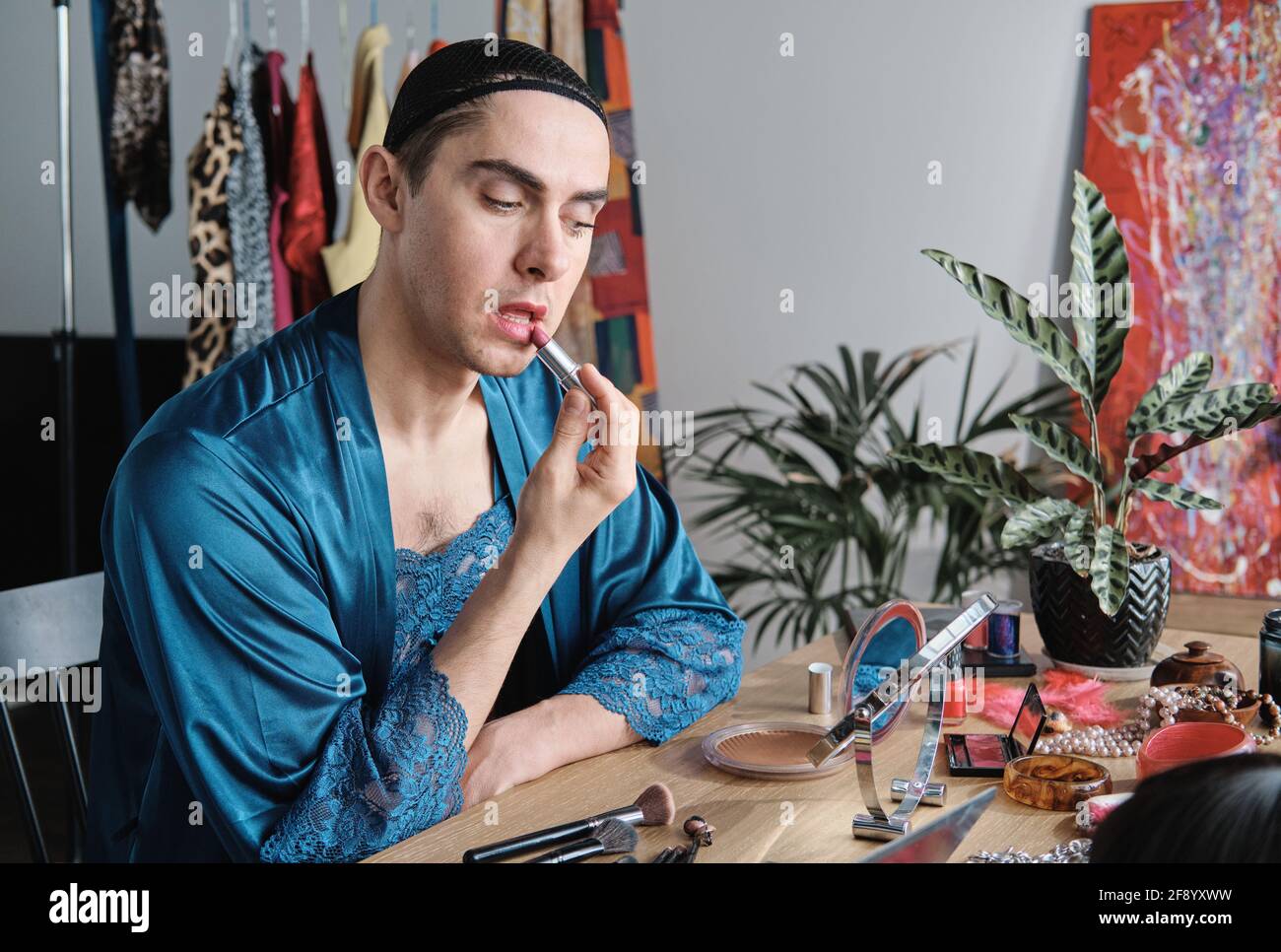 Young man in female dress applying red lipstick and making preparation ...