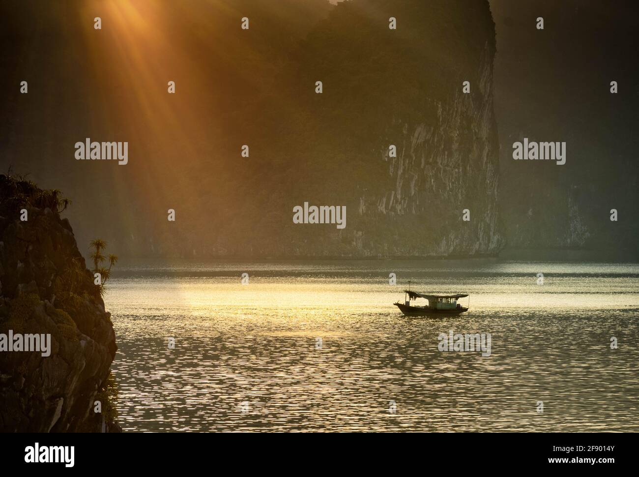 Lone fishing boat in dawn scene in Ha Long Bay, Vietnam with sun rays ...
