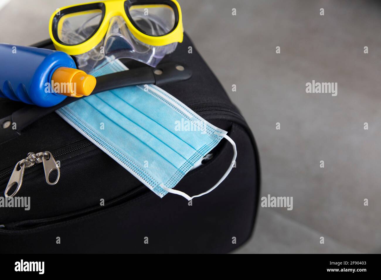 Coronavirus travel. Suitcase with a face mask sun cream and scuba mask ...