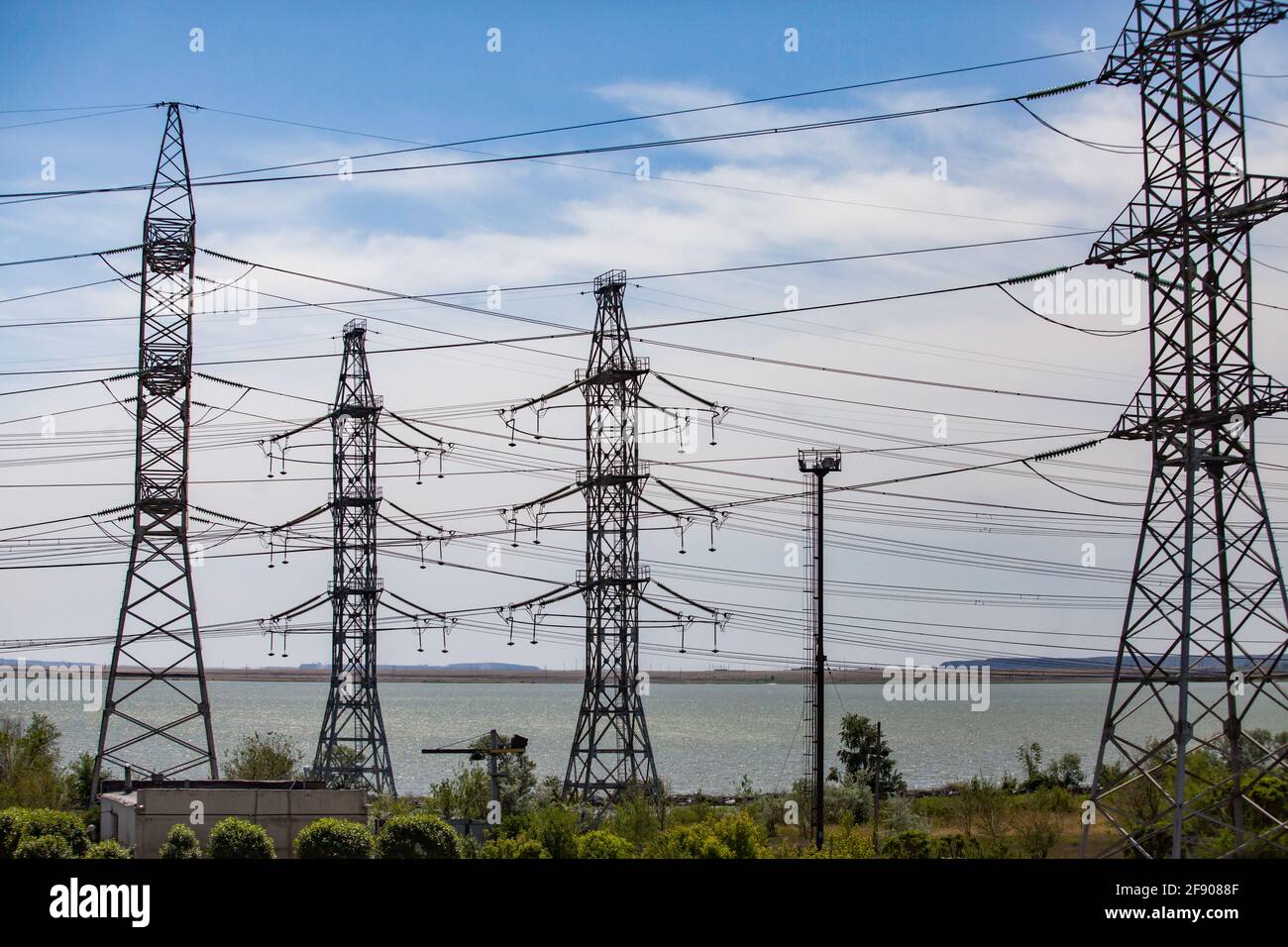High-voltage transmission line and electric pylons on lake and blue sky ...