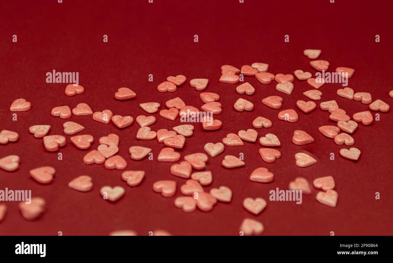 Small sugar hearts are scattered over the surface. Pink hearts on a red ...