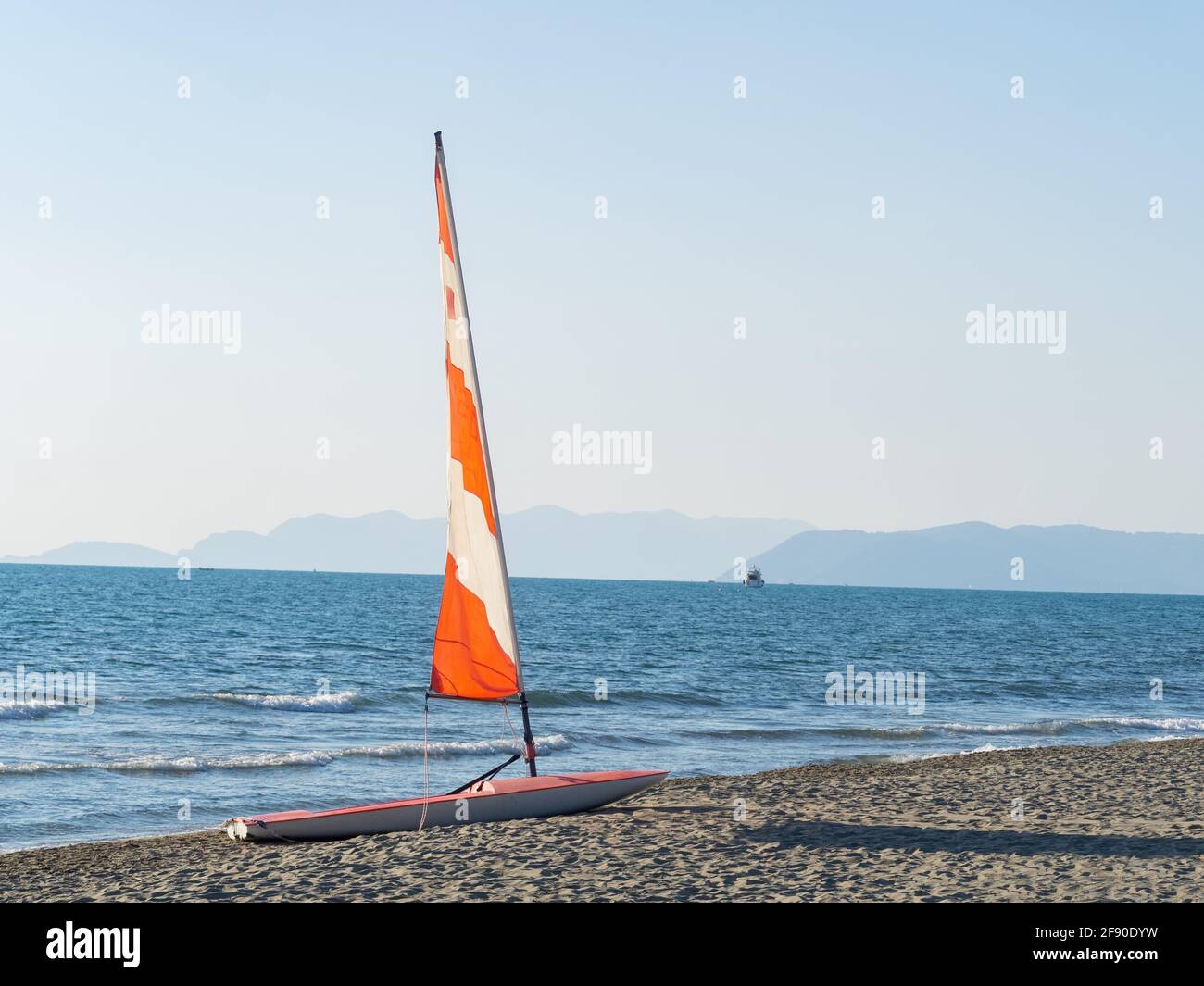 small sailing boat with orange-white striped sail waving in the wind on ...