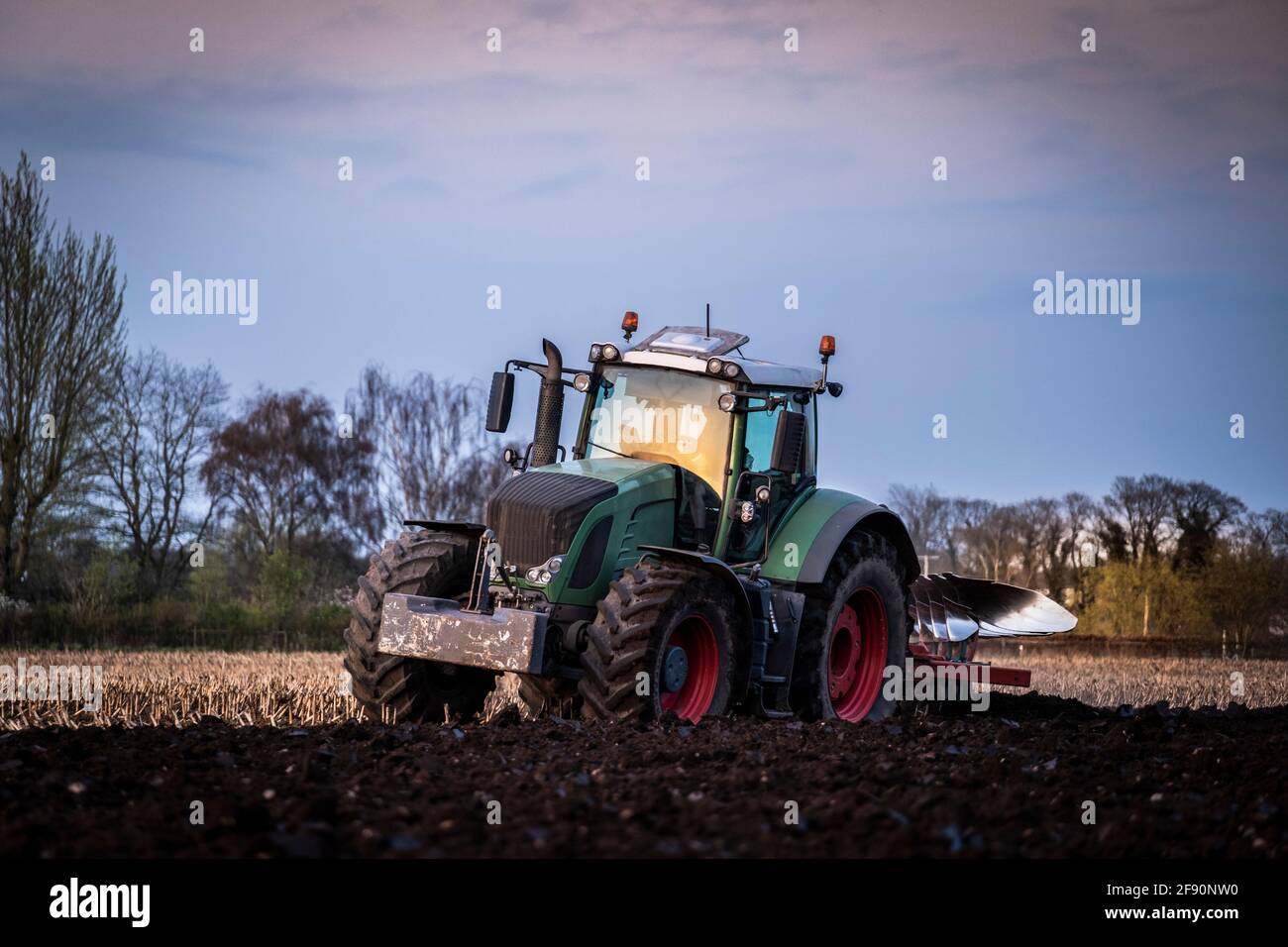 Ploughing a field at sunset with a tractor and plough, ready for crops ...