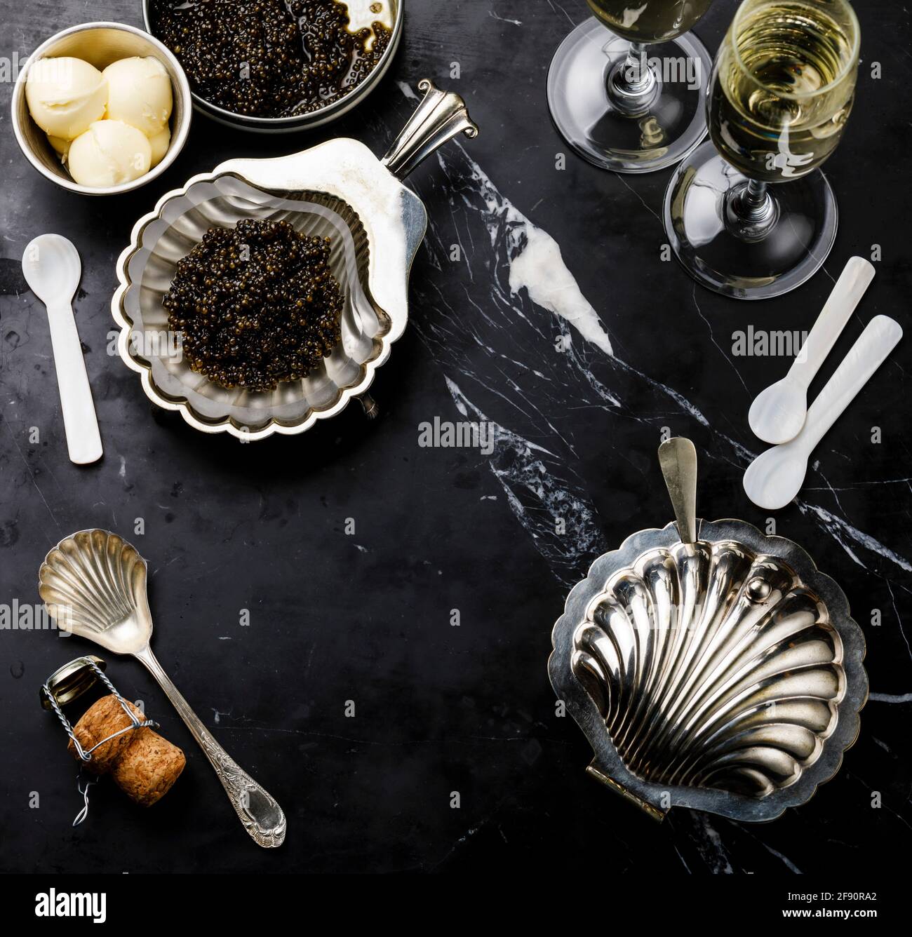 Black caviar in silver bowl and Champagne on black marble background ...