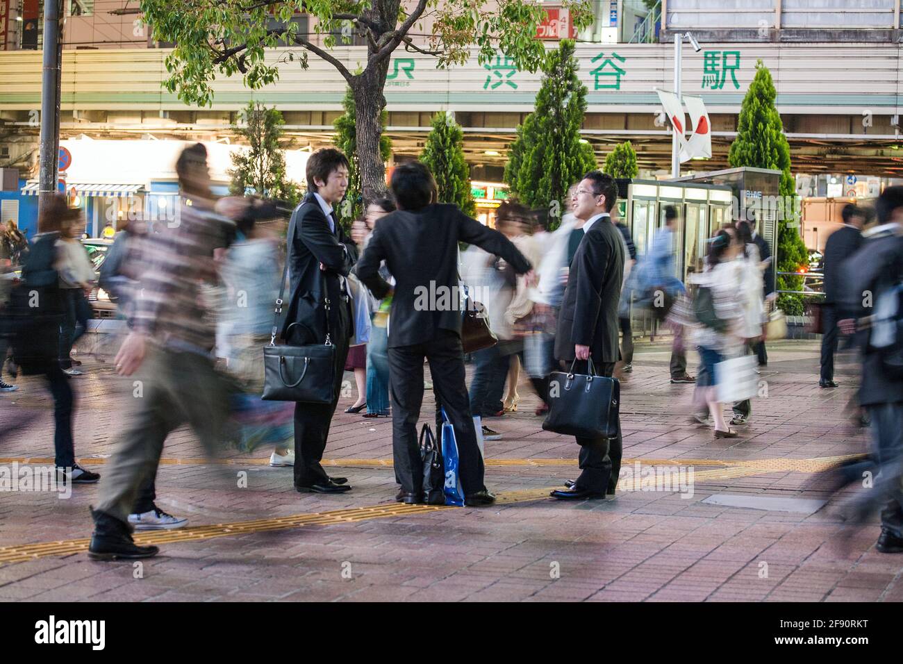 Three Japanese salarymen stand chatting outside Shibuya JR station at ...