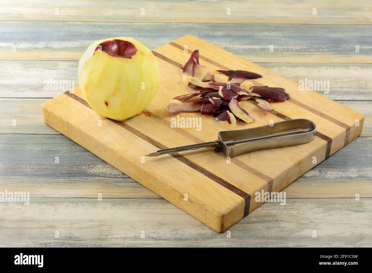 Peeling red delicious apple on wooden cutting board with peels and ...