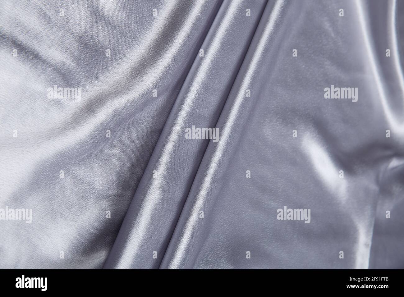 Colored silver textile satin fabric folded in folds and waves with ...