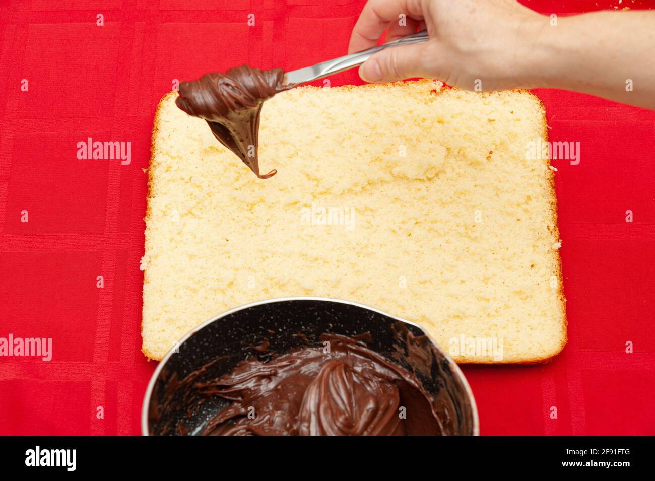 Hand stuffing homemade cake with chocolate ganache. Isolated on red ...