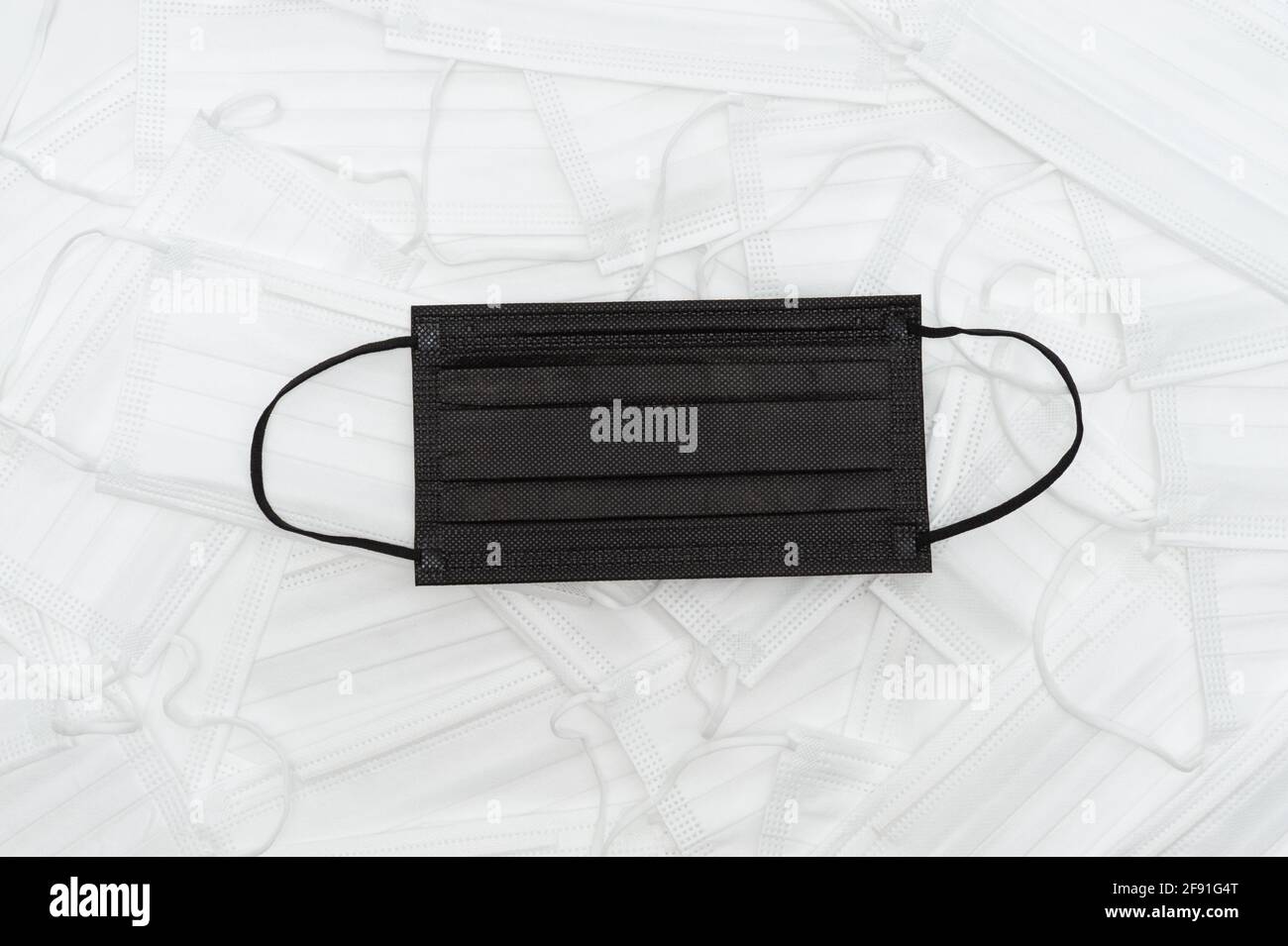 Black surgical mask with a background of scattered white surgical masks ...