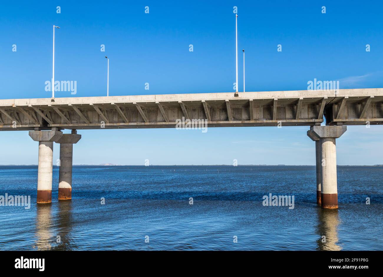 Concrete bridge over the blue ocean with round rusted pillars on a ...