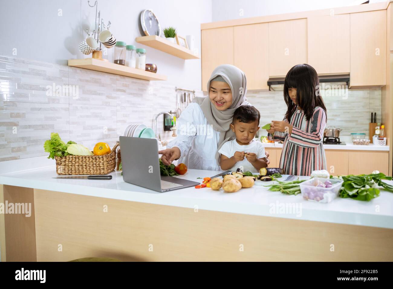 muslim mother watching cooking video on laptop and making dinner with ...