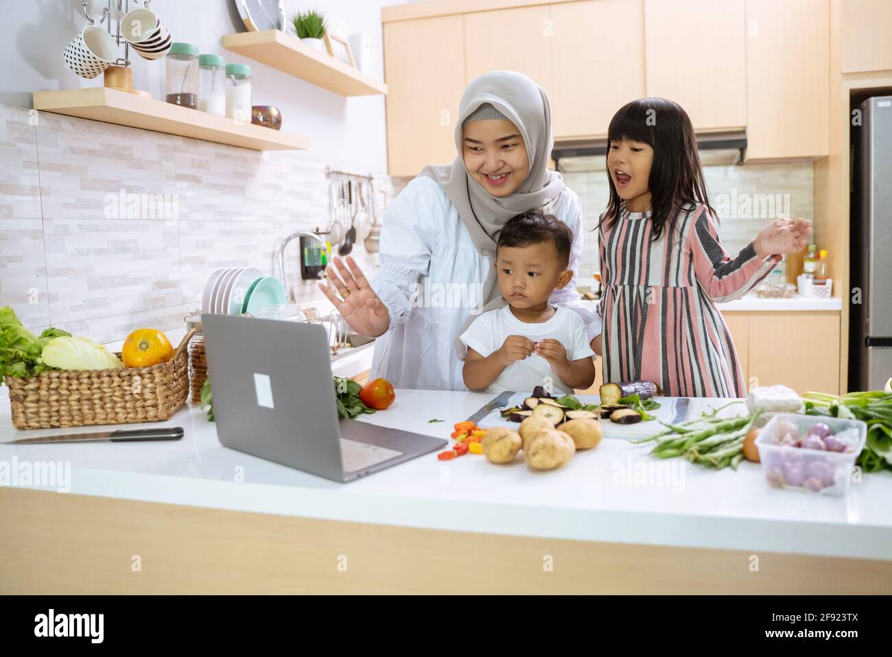 muslim mother watching cooking video on laptop and making dinner with ...