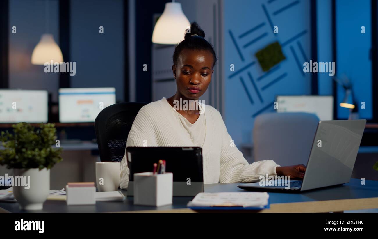 Multitasking black business woman working at laptop and tablet in same ...