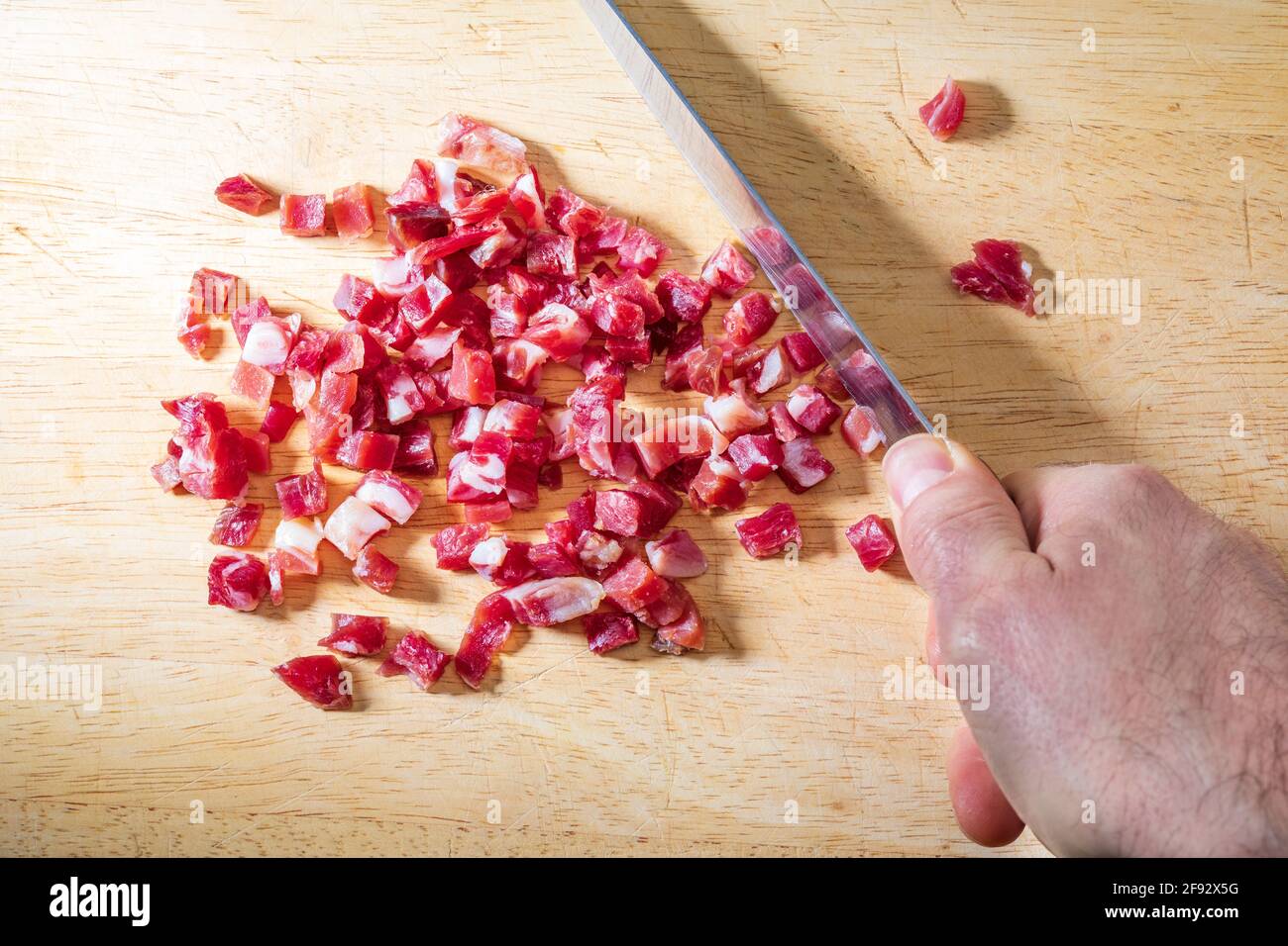 Iberian ham (serrano) cut into cubes (diced). Hand cutting on wooden ...