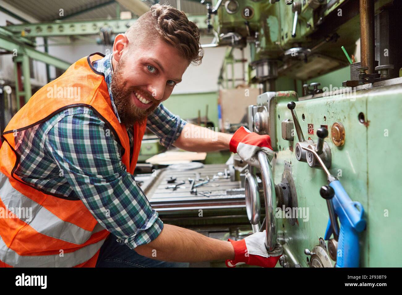 Smiling worker in metal factory operates drill press on a large wheel ...