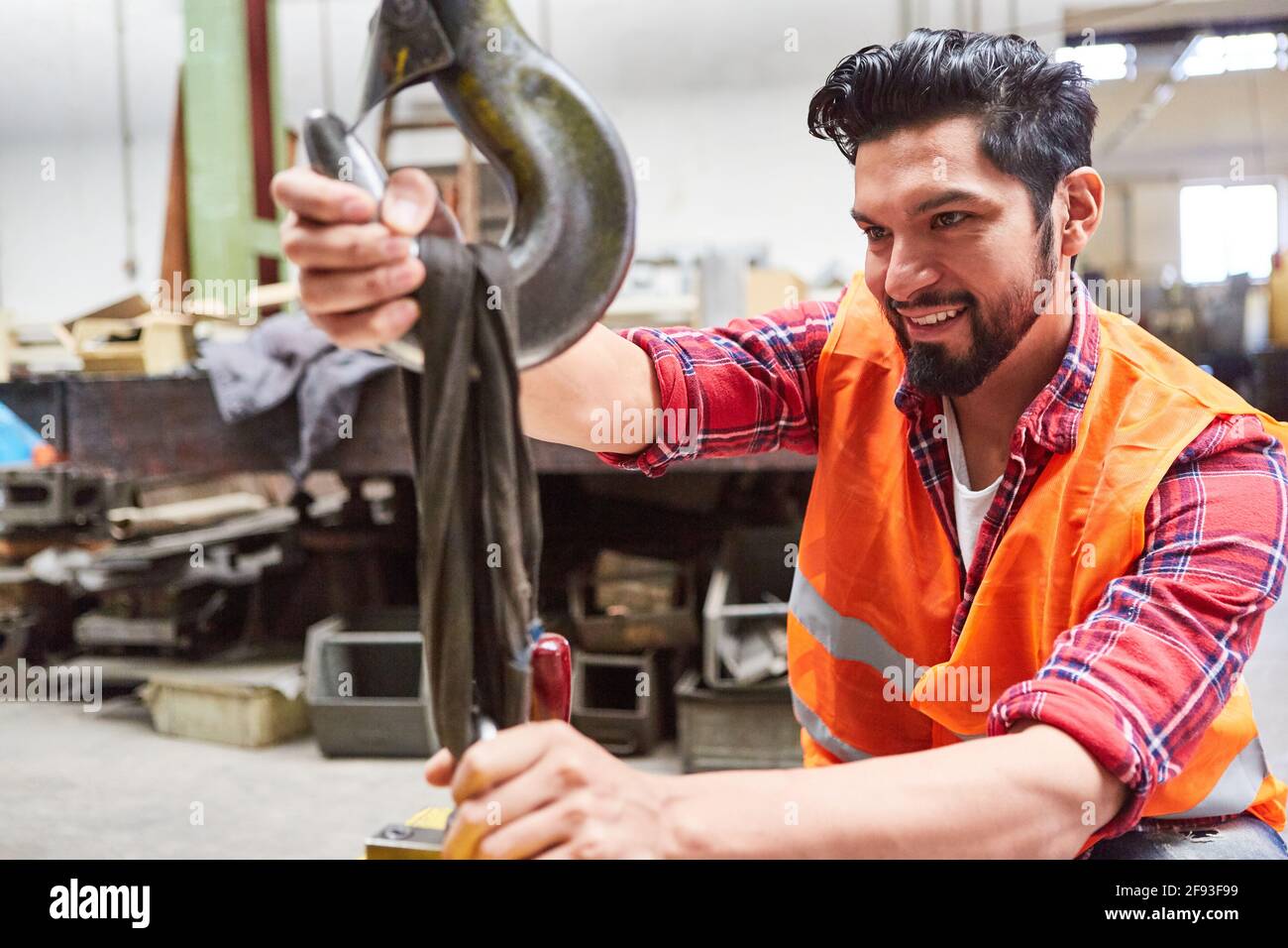 Worker in a factory attaches load to a crane hook in the warehouse or ...