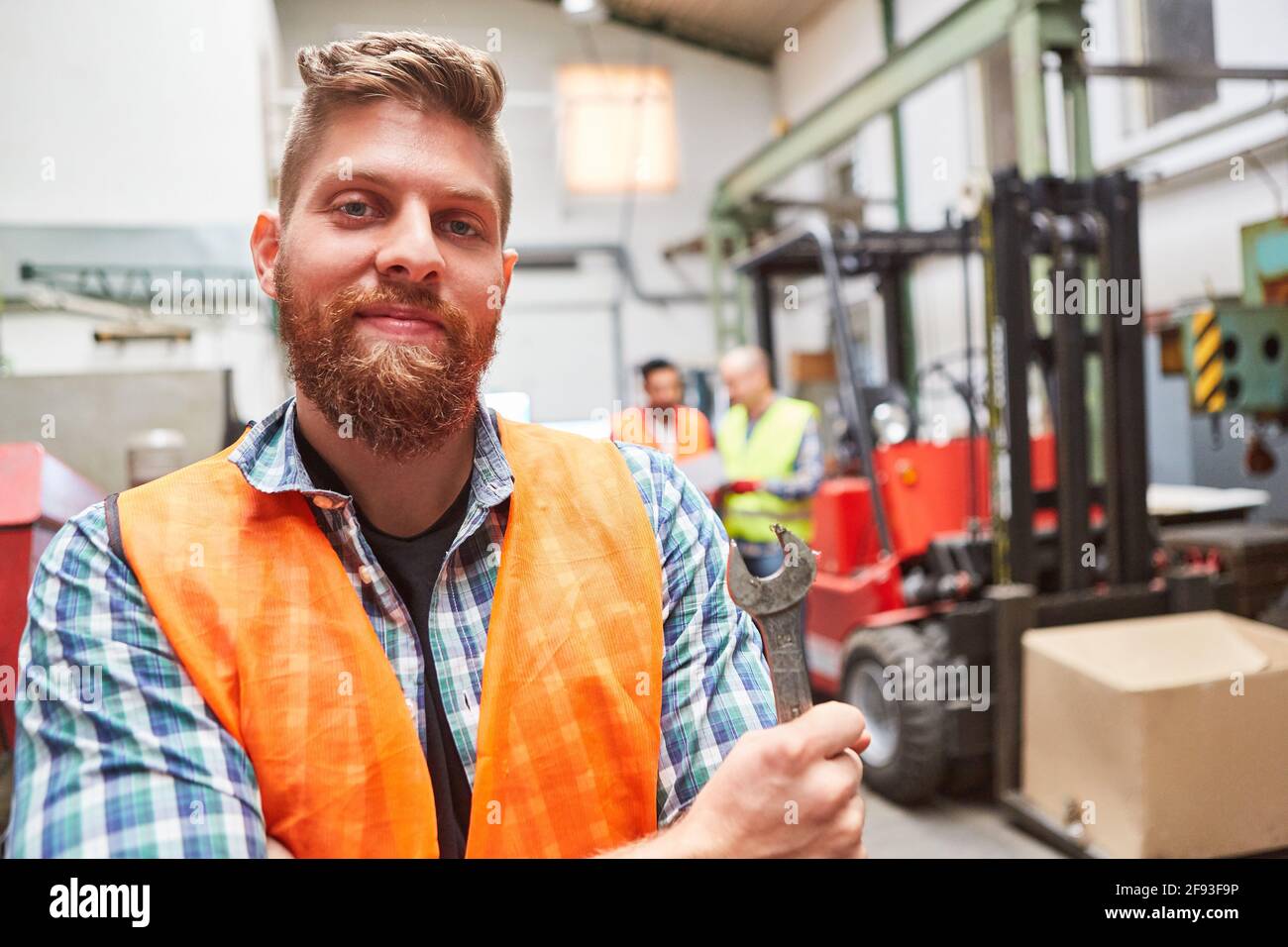 Man as proud warehouse worker with wrench with forklift in background ...