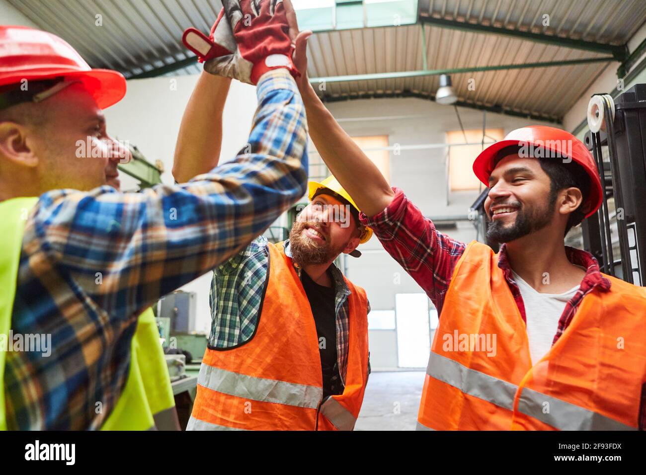 Three industrial workers and craftsmen greet each other with high five ...
