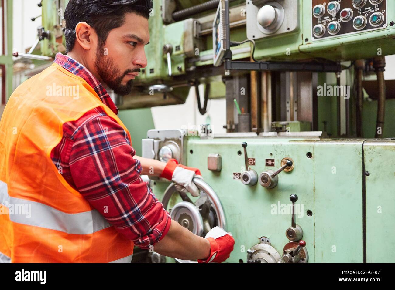 Worker in metal construction factory operates a drill press using a ...