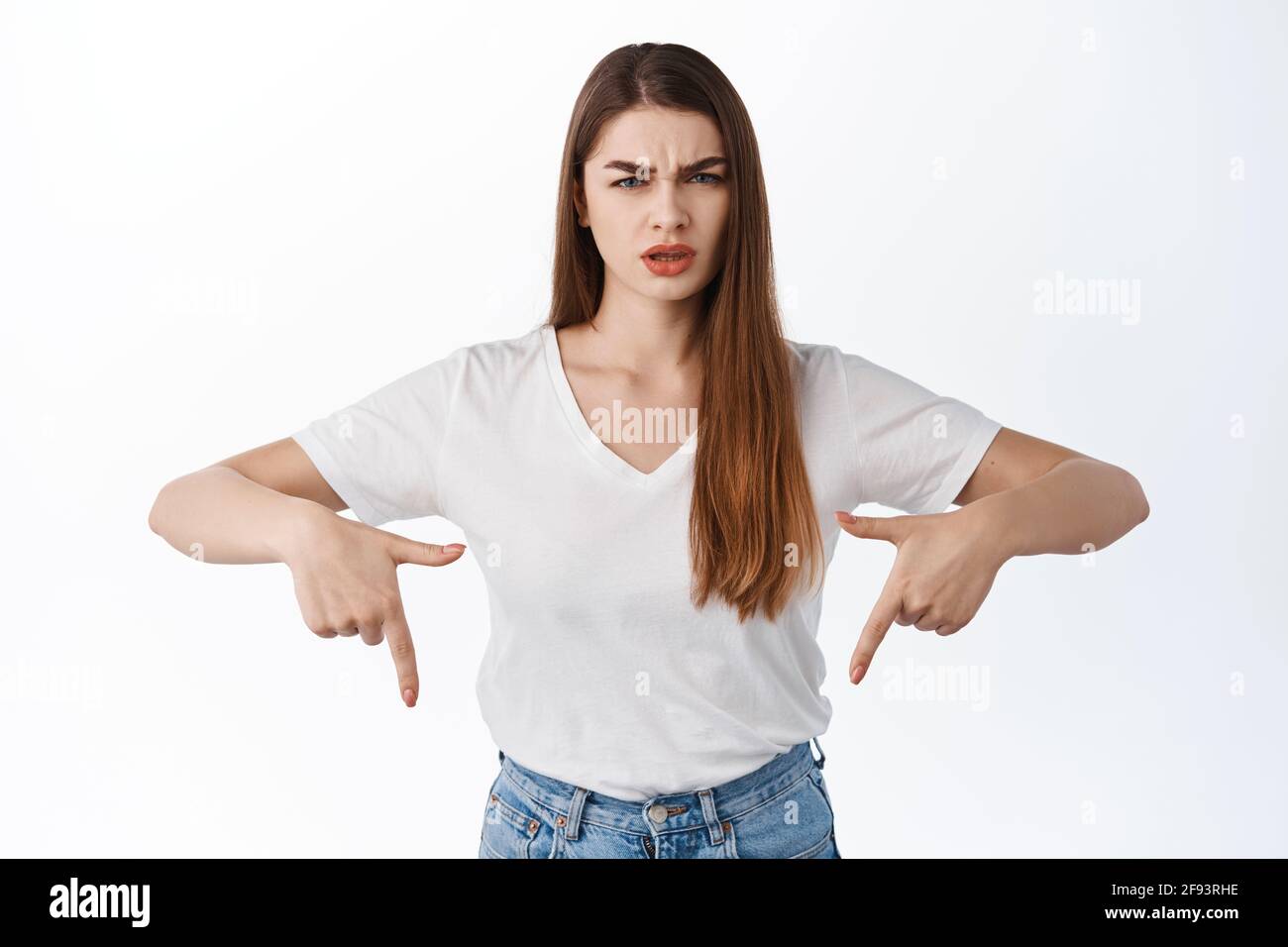 Confused young woman pointing down, looking with frustrated and puzzled ...