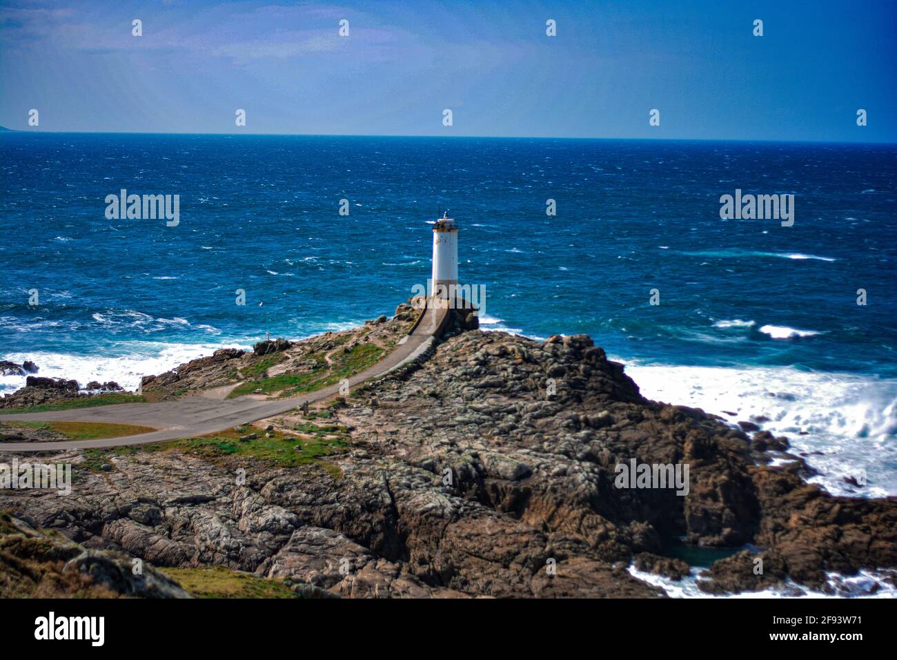 Aerial shot of a lighthouse on rock cliffs with the blue ocean in the ...