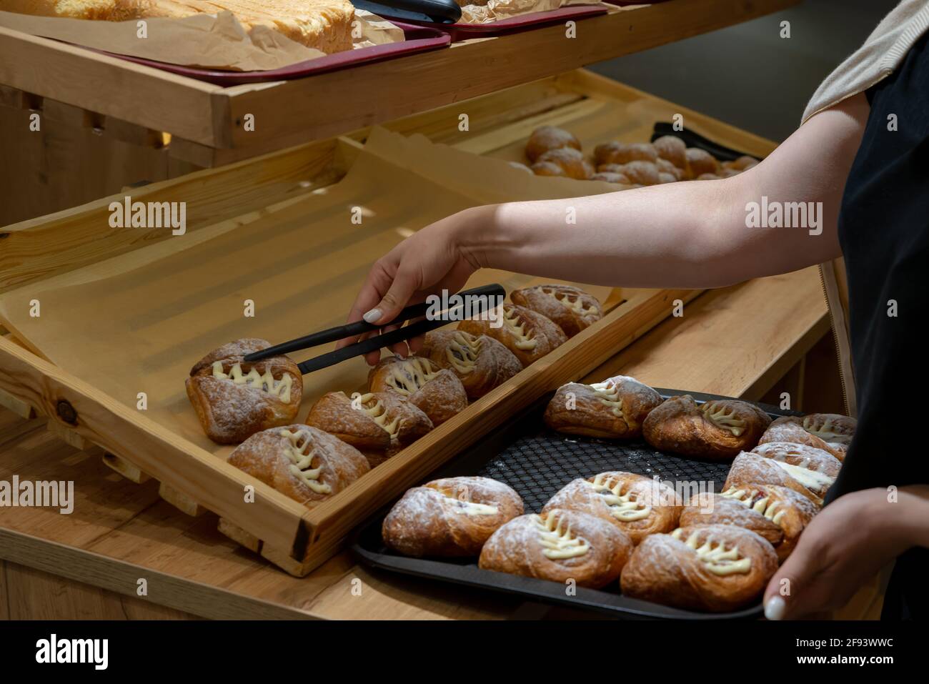 An employee of a bakery, self-service restaurant, lays out buns on a ...
