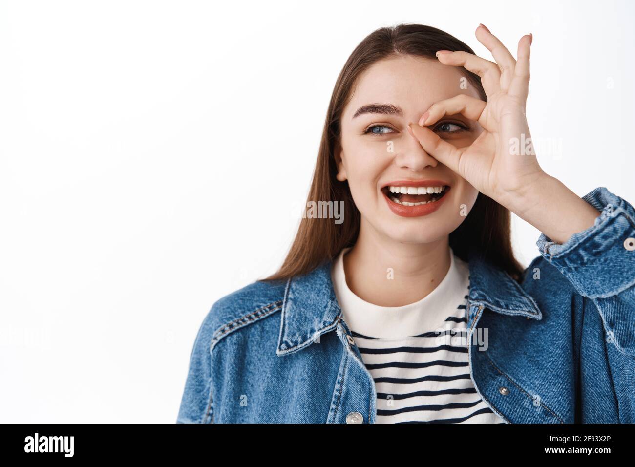 Happy smiling teen girl shows okay sign over eye, laughs and looks ...