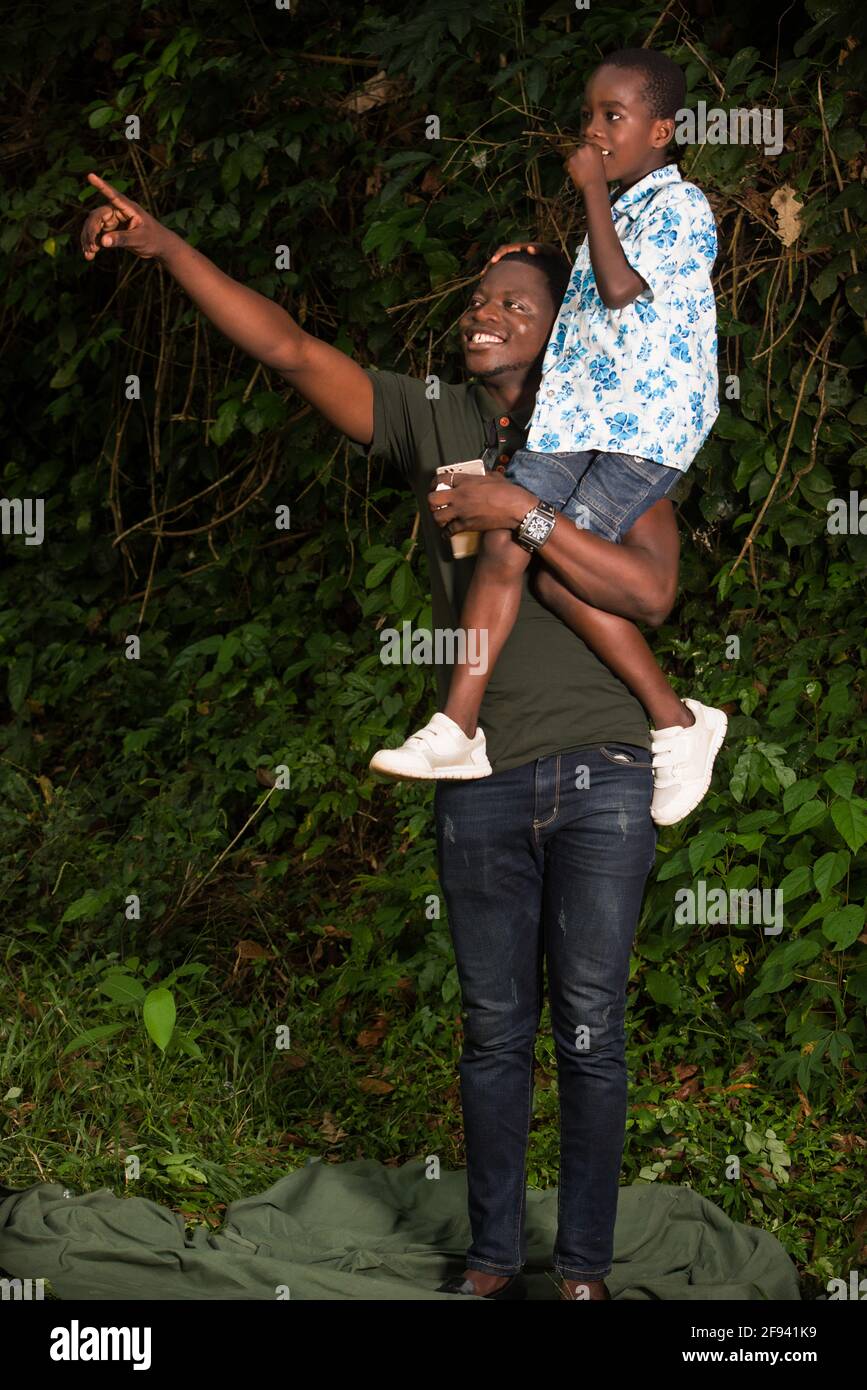 a young man standing in a park with his child on his shoulder showing ...