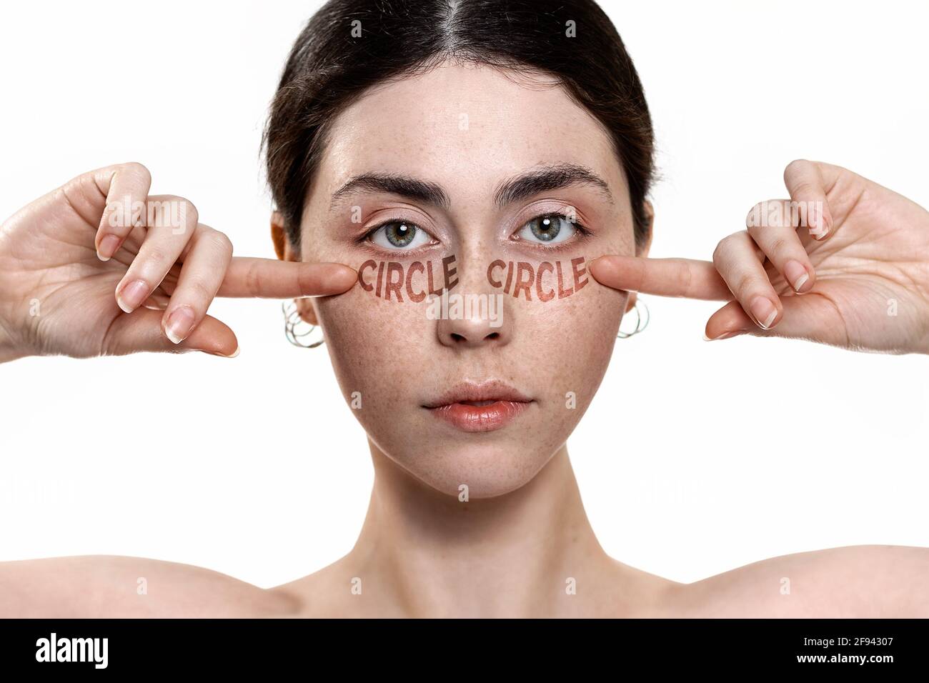 Close-up portrait of a young woman pointing at dark circles under her ...