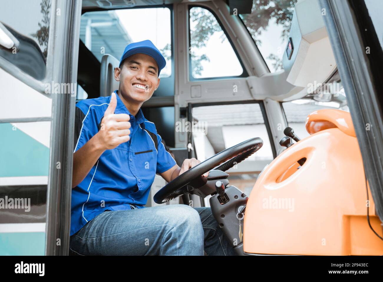 A male driver in uniform smiles at the camera with thumbs up while ...