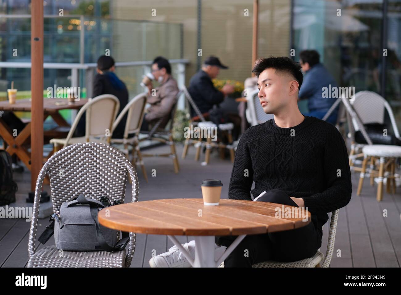 handsome Asian young man sitting at open-air cafe, side face looking ...