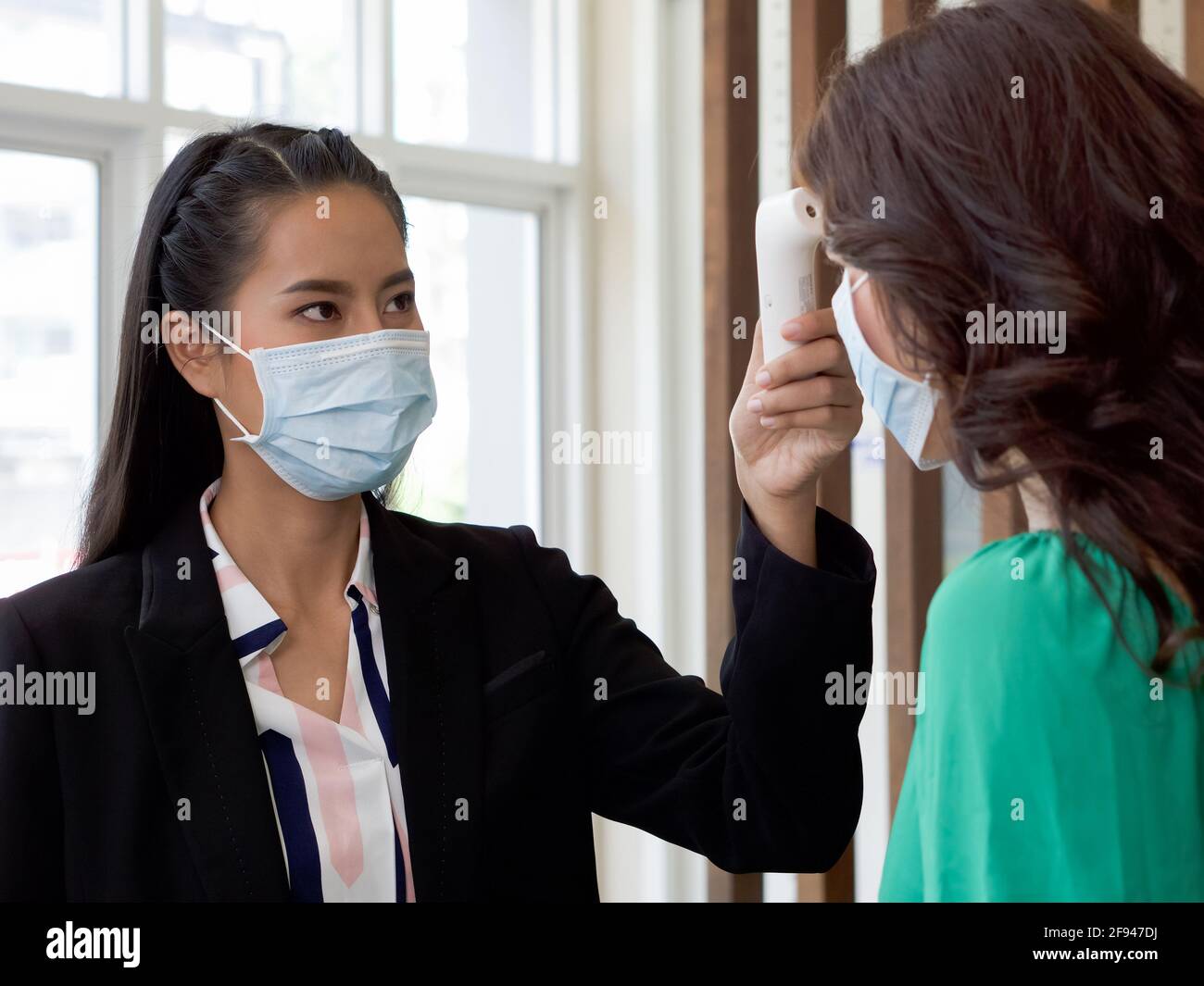 Hotel receptionist in black suit measuring tourist temperature with a ...