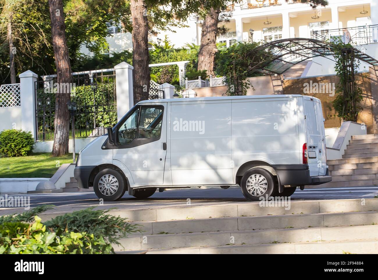 White van is parked in shade of trees on pavement at entrance to ...