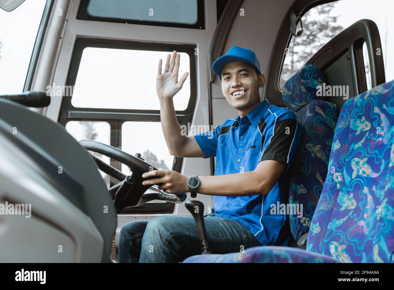 A male driver in uniform smiles at the camera as he sits down and waves ...