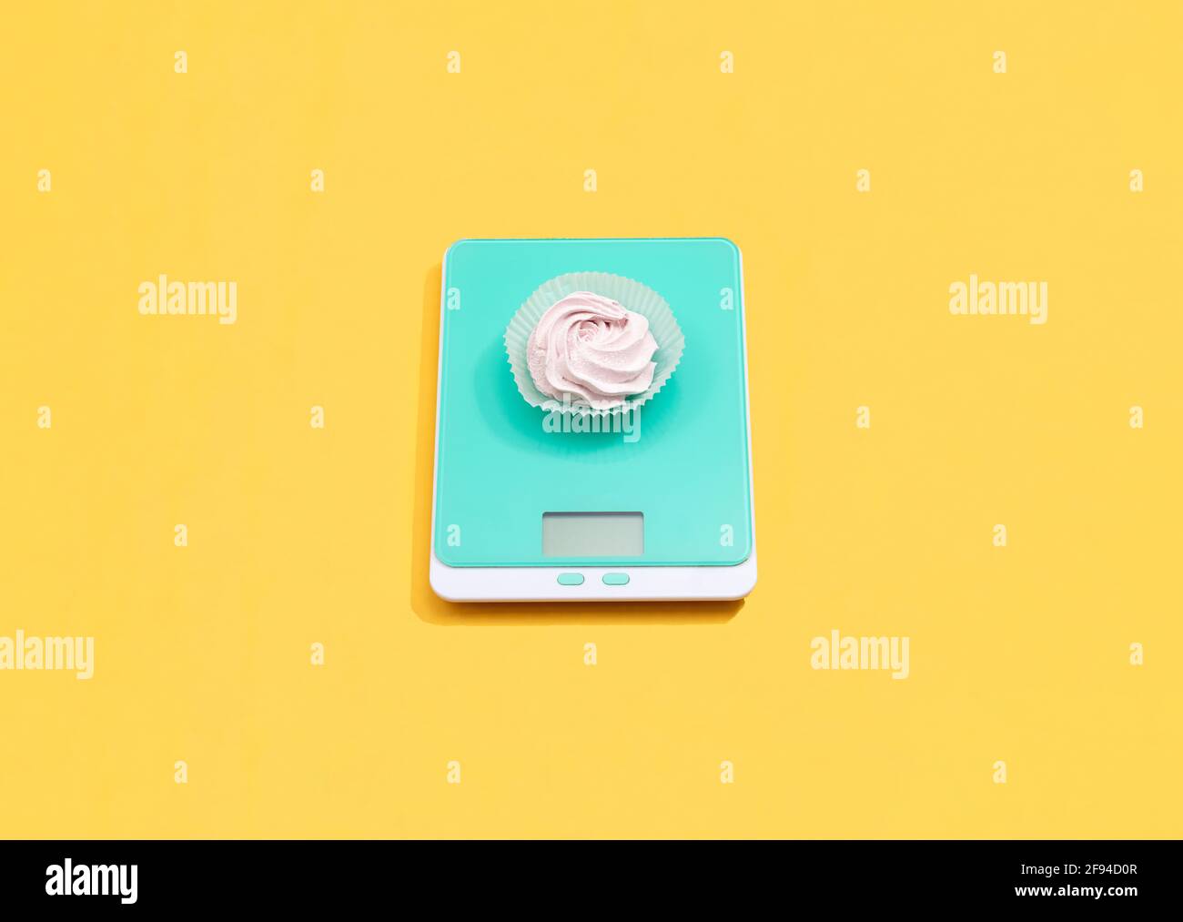 A pink marshmallow lies on an electronic scale on a yellow background ...