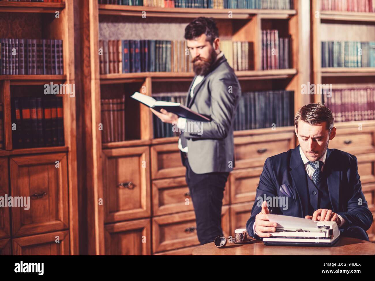 young oldfashioned writer with typewriter in library with bearded ...