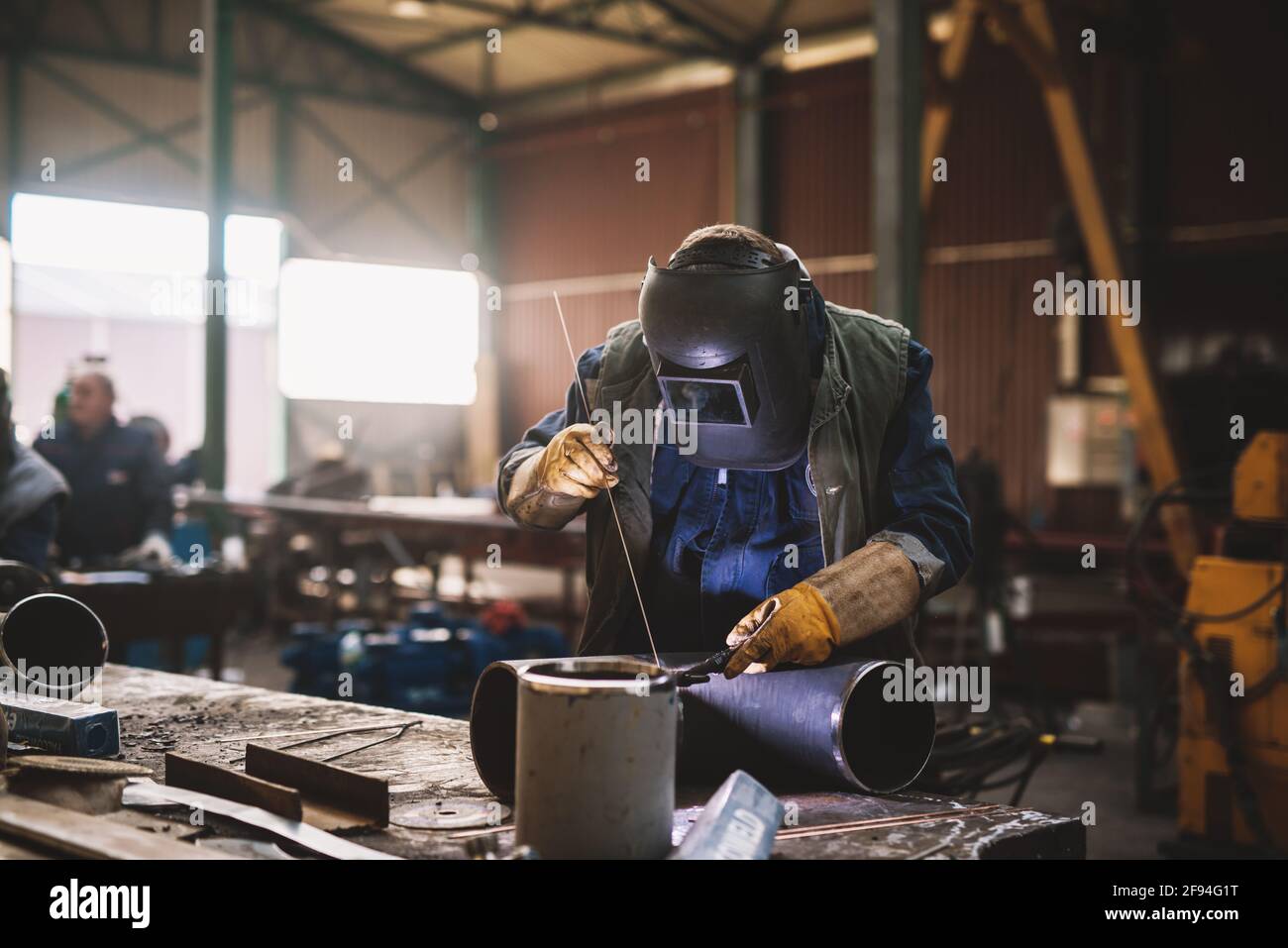 Welder in protective uniform and mask welding metal pipe on the ...
