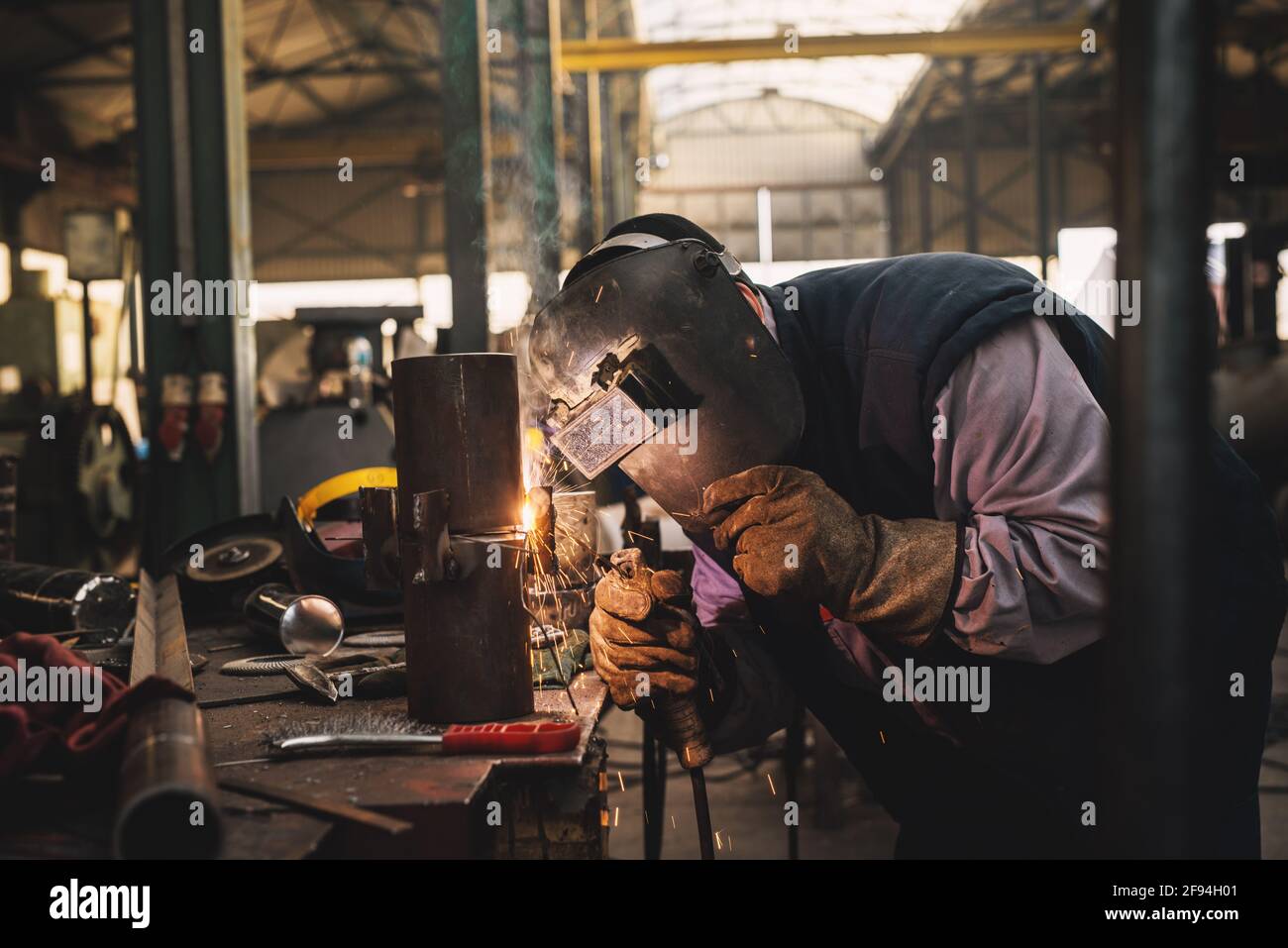 Welder in protective uniform and mask welding metal pipe on the ...