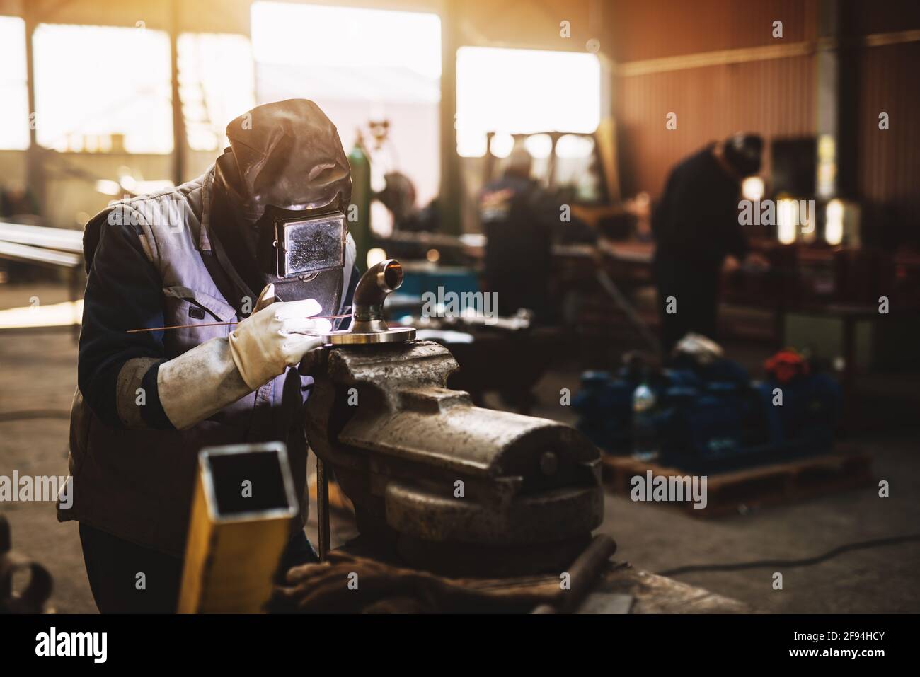 Welder in protective uniform and mask welding metal pipe on the ...