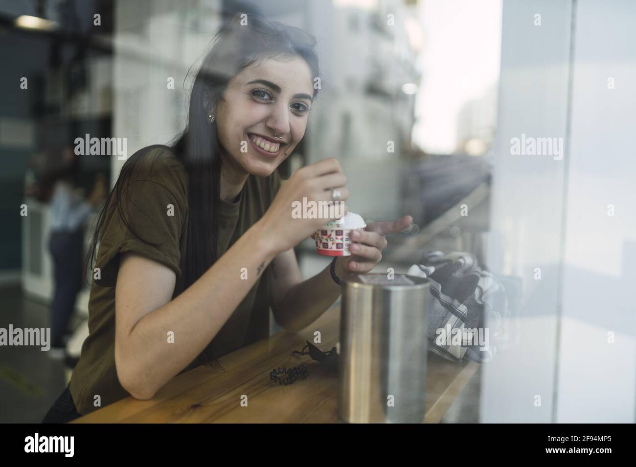 Smiling Spanish female holding ice cream in a cafe behind a window ...