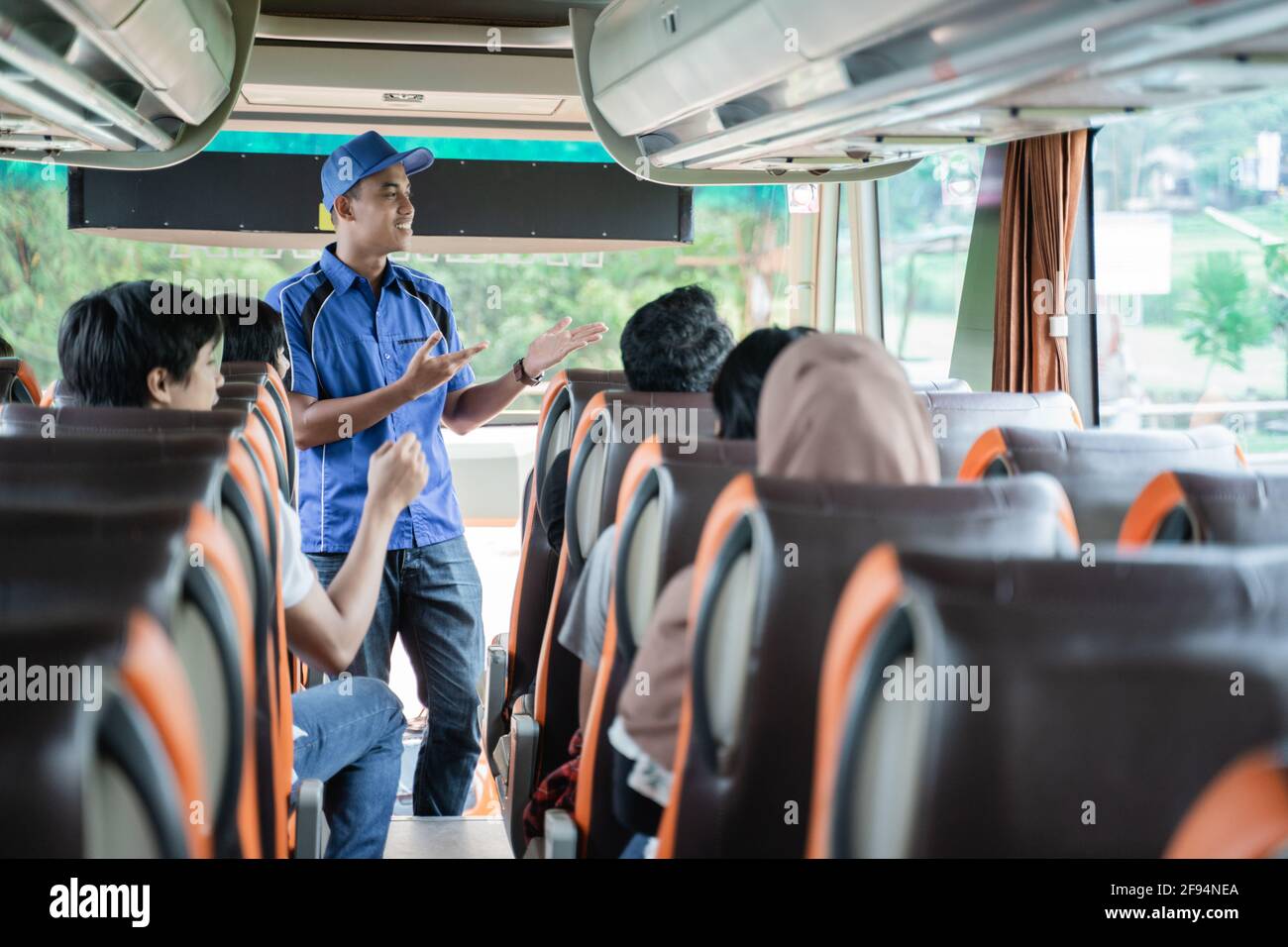 A male bus crew in uniform and a hat briefs passengers with hands-on ...