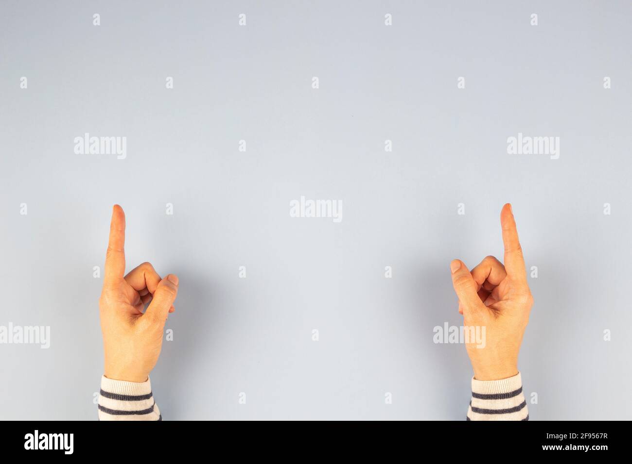 Female hands pointing up with index finger over light gray background ...