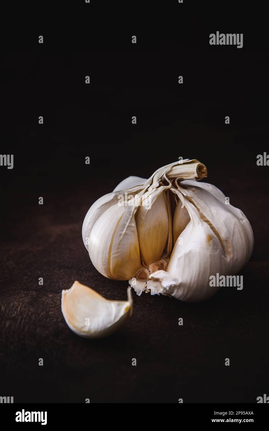 Single garlic bulb with one separated clove on a dark brown background ...
