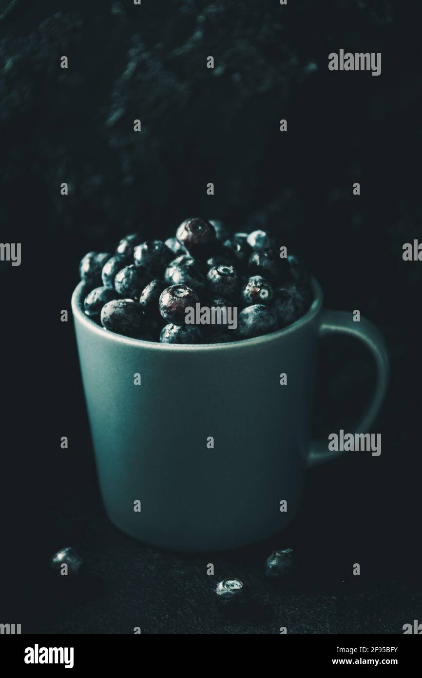 Blue-grey cup filled with ripe blueberries, three of them lying on the ...