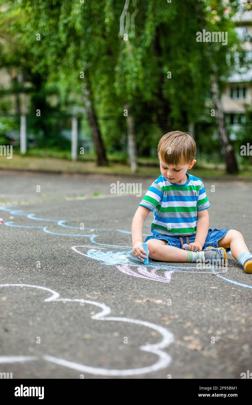Cute boy and girl drawing with chalk on the sidewalk in the park ...