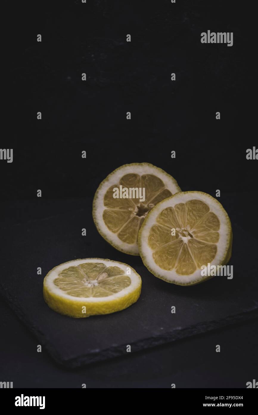 Lemon cut into three pieces, lying on a black slate platter, vertical ...