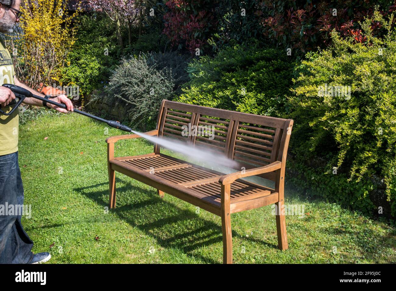 Man cleaning wooden garden bench with a high pressure cleaner in spring ...